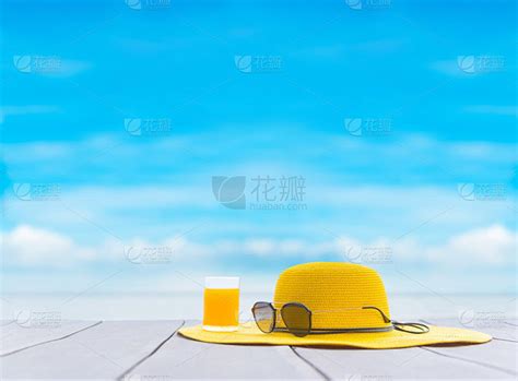 戴着黄色的帽子，在海滩上喝着新鲜的橙汁。暑假与空间在蓝天背景。