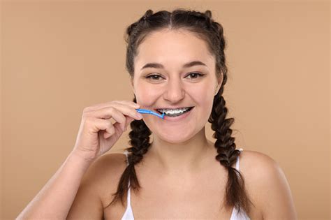 베이지 색 배경에 치간 브러시를 사용하여 치아를 청소하는 치과 교정기를 가진 웃는 여자 25 29세에 대한 스톡 사진 및 기타 이미지 25 29세 개선 건강관리와