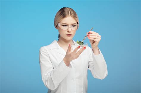 흰색 코트와 파란색 배경에 고글에 젊은 아름 다운 금발 여자 핀셋과 식물의 잎을 보유 하 고 있습니다 과학의 개념 식물과 제품의 연구 Gmo 테스트 과학자 생물학자 이자