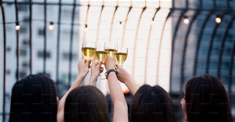 옥상 레스토랑에서 파티를 하는 젊은 아시아의 귀여운 여성들 화이트 와인 술을 마시고 잔을 건배하는 소녀들은 행복을 느끼며 뒤에서 본 재미를 느낍니다 밤 라이프 스타일