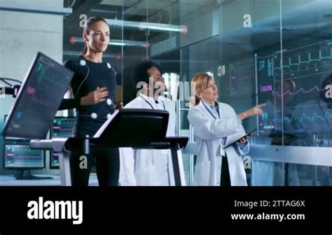 Beautiful Woman Athlete Runs On A Treadmill With Electrodes Attached To Her Body While Two