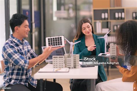 풍력 터빈과 함께 만나는 엔지니어 팀은 풍력 터빈과 함께 태양 전지판이 있는 테이블 위에 놓인 주택 모델과 청사진을 사용하여 풍력과 태양열을 사용하여 재생 에너지를