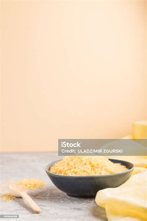 회색과 주황색 배경과 노란색 직물에 원시 황금 쌀과 나무 숟가락과 파란색 세라믹 그릇 측면 보기 선택적 초점 복사 공간 0명에 대한 스톡 사진 및 기타 이미지 Istock