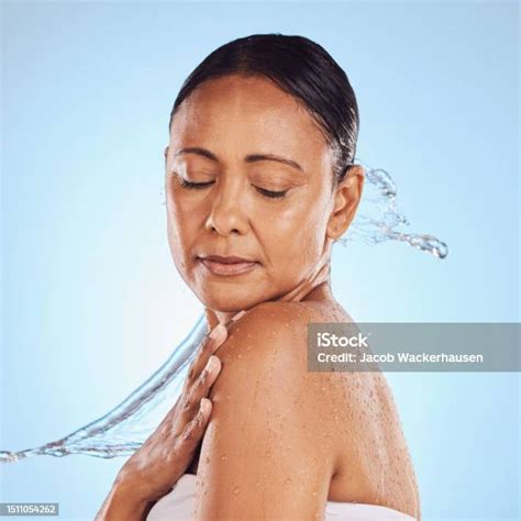 스킨케어 샤워 그리고 스튜디오의 파란색 배경에 고립된 물이 튀는 성숙한 여성 글로우 안티에이징 및 피부 그루밍 및 위생을 위한 수분 액체 및 액체가 있는 모델 50 54세에