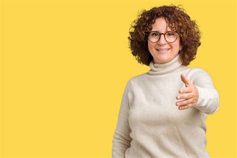 아름 다운 중간 어른 고위 여자 웃 고 인사 하 고 환영으로 제공 하는 친절 한 악수 하는 격리 된 배경 위에 터틀 넥 스웨터와 안경 착용 성공적인 사업입니다 악수에 대한