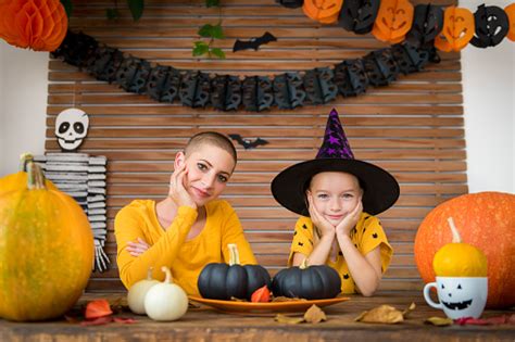 귀여운 어린 소녀와 그녀의 어머니 암 환자 할로윈 테마에서 테이블 뒤에 앉아 카메라를 보고 웃 고 룸 장식 가족 할로윈 생활양식입니다 2명에 대한 스톡 사진 및 기타 이미지