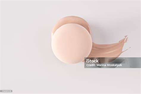 둥근 화장품 스펀지가 자연스러운 톤의 파운데이션 리퀴드 파우더 스트로크 위에 얹혀 있습니다 평면도 흰색 배경입니다 복사 공간입니다 보살핌과 아름다움 갈색에 대한 스톡 사진