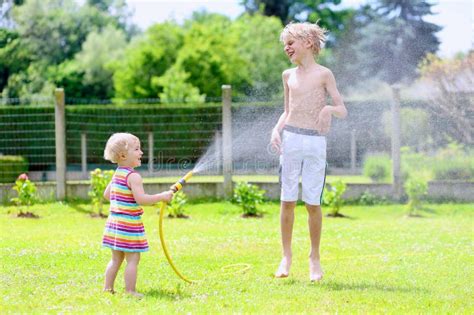 Il Fratello E La Sorella Che Giocano Con Acqua Annaffiano Nel Giardino