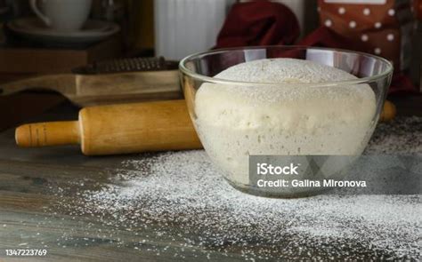 베이킹 효모 반죽 발효 오파라를 흰 밀가루로 가루로 한 테이블에 있는 그릇에 사워도우 나무 롤링 핀과 배경에 부엌 기구 수제 빵 피자 파이를 요리하는 과정 신 반죽 건강한