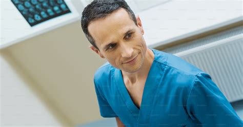 즐거운 일꾼 Ct 스캔 실험실에 서서 먼 곳을 바라보며 웃고 있는 남자 간호사의 파란색 유니폼을 입은 잘 생긴 중년 남자 사진 Unsplash의 남자 간호사 이미지