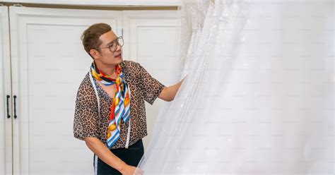 아시아 Lgbtq 남자 신부 가게 주인은 웨딩 스튜디오의 탈의실에서 여성 신부 고객을 위해 옷걸이에 걸려 웨딩 드레스를 선택합니다 중소 기업 기업가 웨딩 플래너 및 재단사