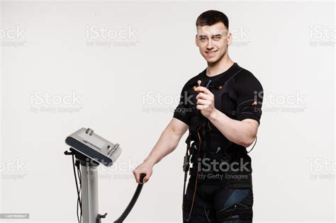 Ems를 입은 근육질의 남성 운동선수는 흰색 배경에 근육을 자극하기 위해 전기 충격을 사용하는 접촉기를 손에 들고 있다 전기