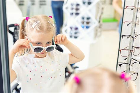 귀여운 젊은 백인 금발 소녀에 시도하고 광학 안경 가게에서 거울 앞에서 선글라스를 선택합니다 사랑스러운 여학생 아이 재미 에 의해 태양 자외선 차단 안경 에 가게 거울에
