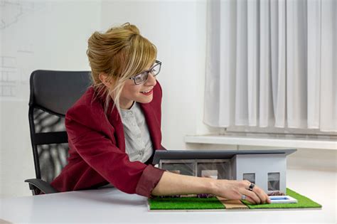 사무실에서 젊은 여성 건축가는 집 모델을 보고 책상에 앉아 프로젝트에 대 한 생각 안경으로 사려 깊은 디자이너 건물 외관에 대한 스톡 사진 및 기타 이미지 Istock