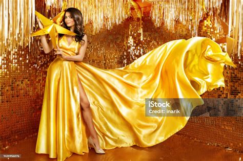 바람에 날아 다니는 황금 실크 드레스의 패션 모델 옐로우 롱 가운에 아름다운 여자가 빅 골드 스타를 들고 있습니다 골든 파티