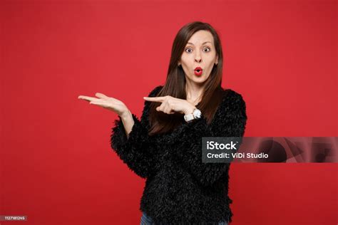 검은 모피 스웨터 포인팅 검지 손가락 손 옆으로 스튜디오에서 밝은 빨간 벽 배경에 고립에 충격된 젊은 여자의 초상화 사람들이 진심으 감정 라이프 스타일 개념 복사 공간을