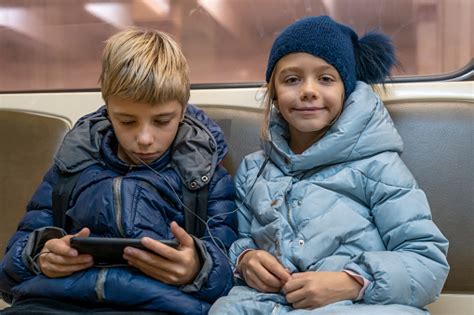 헤드폰을 장착한 어린이들이 도시 지하 열차에서 휴대전화로 비디오를 시청하고 있습니다 지하 교통에서 휴대 전화에서 비디오를 스트리밍하기위한 인터넷 기술 가는 길에 의식적인