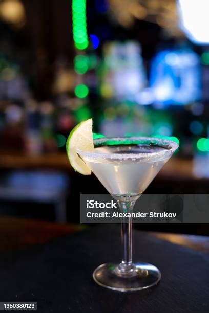 긴 줄기가 있는 깔때기 모양의 유리에서 알코올 칵테일은 불투명하고 불투명하며 유리의 설탕 가장자리에 라임 조각이 있습니다 보케의 밝은 조명의 배경에 대한 바 메뉴의 촬영 0