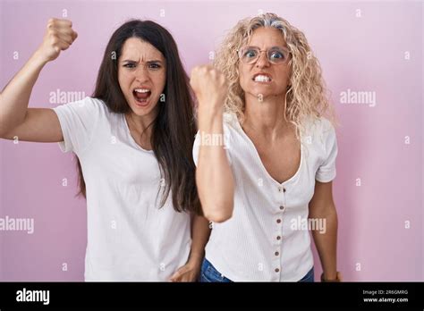 Mother And Daughter Standing Together Over Pink Background Angry And