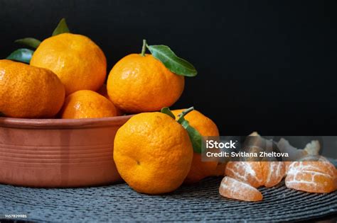 신선한 익은 오렌지 만다린 클레멘 타인 테이블 위의 그릇에 나뭇잎이있는 감귤 검은 배경의 회색 플레이스 매트에 껍질을 벗긴 얇게