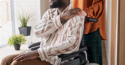 뒤에 서 있는 백인 여성 간병인의 손에 손을 얹고 있는 장애가 있는 젊은 아프리카계 미국인 남성의 측면 모습 사진 Unsplash의 휠체어 이미지