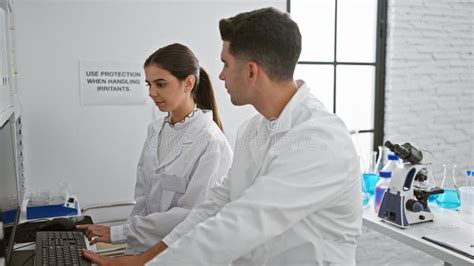 A Man And Woman Dressed As Scientists Work Together At A Computer In A Modern Laboratory