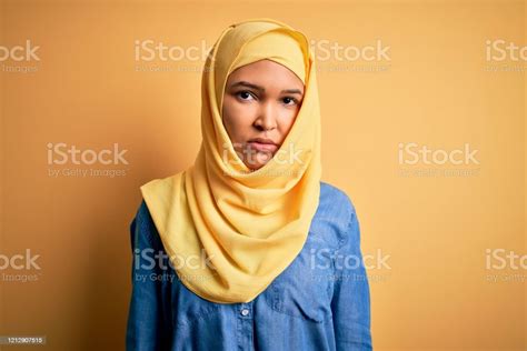 젊은 아름 다운 여자 곱슬 머리를 입고 아랍 전통 히잡 위에 노란색 배경 얼굴에 심각한 표정으로 편안 카메라를 보는 간단하고 자연스러운 슬픔에 대한 스톡 사진 및 기타