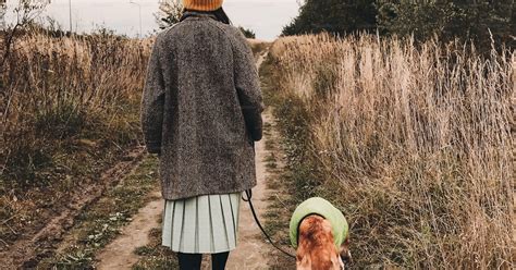 노란 모자와 코트를 입은 세련된 힙스터 소녀는 허브 사이에서 가을 들판에서 코트를 입은 황금 개와 함께 걷고 있습니다 시골에서