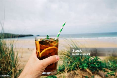 여름날 뉴퀘이 주피스트랄 비치 위의 민트와 레몬을 곁들인 아이스 티 잔을 들고 있는 손의 Pov 아이스 티에 대한 스톡 사진 및 기타 이미지 Istock