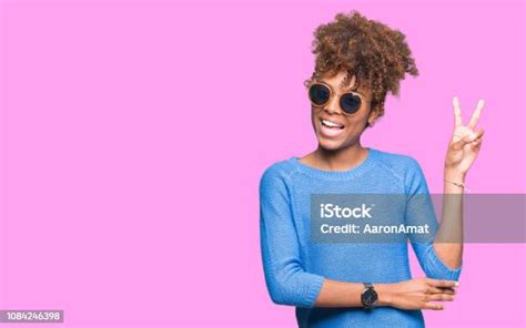 아름 다운 젊은 아프리카계 미국인 여자 승리 표시를 하 고 카메라에 윙크 하는 행복 한 얼굴로 웃 고 고립 된 배경 위에 선글라스를 착용 번호 2입니다 눈 신체 부분에 대한