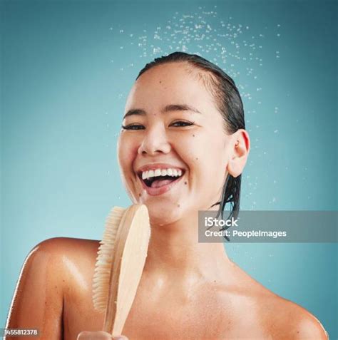 스튜디오에서 청소 웰빙 및 피부 각질 제거 미용 및 손질을 위해 샤워를 하는 초상화 목욕 브러시 및 여성 스킨케어 물 튀김 및 아시아 모델 세탁의 얼굴 파란색 배경에서 휴식