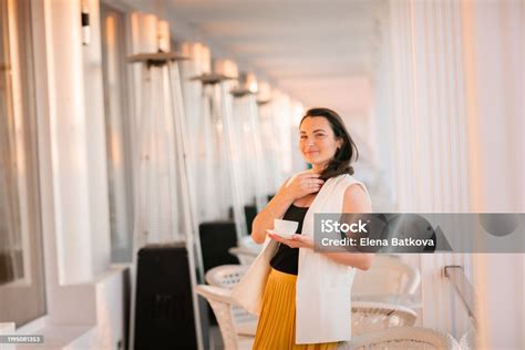 카푸치노 컵을 손에 들고 카페에서 포즈를 취한 노란 드레스의 세련된 미국 여성 갈색 머리에 대한 스톡 사진 및 기타 이미지