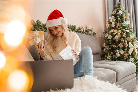 온라인 크리스마스 인사말 하얀 스웨터와 빨간 산타 모자를 쓴 여성은 노트북을 사용하여 친구 부모 및 온라인 쇼핑을 위해 화상 통화를합니다 12월에 대한 스톡 사진 및 기타