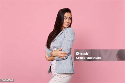 옆으로 보이는 줄무늬 재킷에 예쁜 젊은 여자의 초상화 손을 잡고 스튜디오에서 분홍색 파스텔 벽 배경에 고립 된 교차 사람들은 진심으로 감정 라이프 스타일 개념입니다 복사