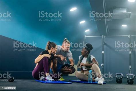 피트니스 체육관 강사는 수건으로 운동복을 입은 두 명의 적합한 여성에게 태블릿에서 운동 계획을 보여줍니다 그들은 운동 후 휴식을 취하면서 체육관 바닥에 앉아 있습니다 25