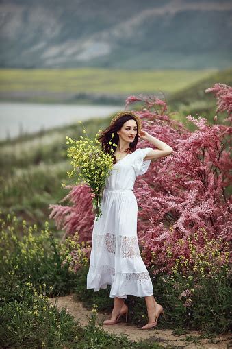 흰색 드레스를 입은 소녀가 노란 들판 꽃다발이 달린 우아한 모자를 쓰고 녹색 들판에 서 있다 귀여운에 대한 스톡 사진 및 기타 이미지 Istock