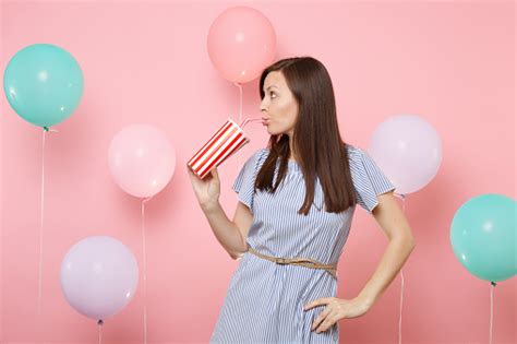 블루 입고 예쁜 여자의 초상화 화려한 공기 풍선 파스텔 핑크 배경에 플라스틱 컵에서 찾고 따로 마시는 콜라 나 소 다를 드레스 생일 휴가 파티 사람들이 진심으 감정 14에