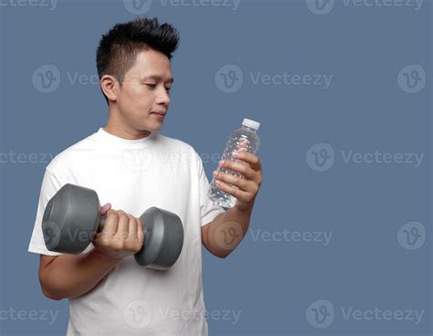 Young Man Holding Dumbbells And Bottled Water Isolated On Plain