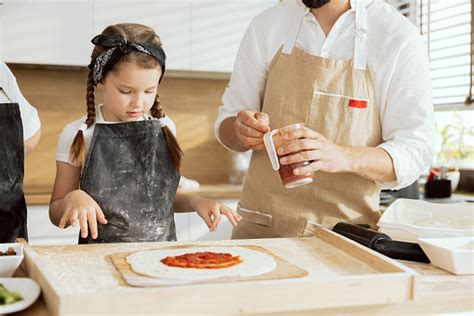 클로즈업 샷은 준비된 롤링 반죽에 토마토 소스를 바르는 앞치마를 입은 사랑스러운 아이를 기뻐했습니다 토마토 소스 케첩으로 측정 컵을 들고있는 아버지의 손 가족에 대한 스톡