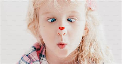 코에 빨간 하트 스티커를 보고 있는 십자형 아이 파란 눈을 가진 재미있는 재미있는 백인 백인 귀여운 사랑스러운 아이 소녀