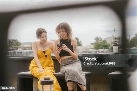 두 명의 아시아 여성이 카페에서 수다를 떨고 스마트폰으로 사진을 보여주고 있다 둘 다 웃는다 2명에 대한 스톡 사진 및 기타