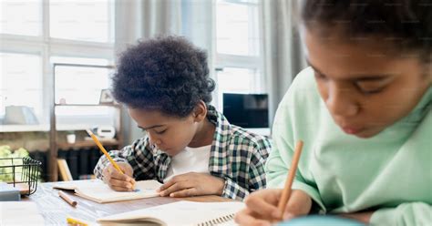 캐주얼 차림의 귀여운 초등학생과 그의 여동생은 가정 환경에서 테이블 옆에서 숙제를 하면서 카피북에 메모를 하고 있다 사진 Unsplash의 틴에이저 이미지