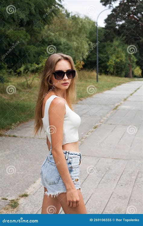 Girl With Long Blond Hair In Short Denim Shorts And A White Top In