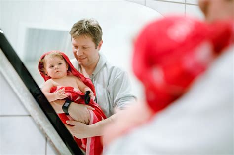 아버지는 목욕을 한 후 수건으로 싸여 귀여운 어린 유아 소녀를 안고 있습니다 욕실과 웃음거울을 보고 젖은 머리카락을 가진 행복한 건강한 아기 아이 딸과 아빠의 가족 관계