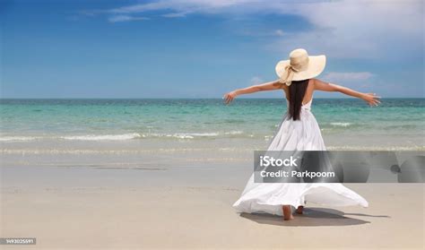 뒷모습은 아름다운 드레스와 모자를 쓰고 모래사장에 서 있는 젊은 행복한 아시아 여행자 여성 귀여운 소녀는 여름과 햇살이 내리쬐는 날에 편안한 휴가를 보내며 열대 바다를
