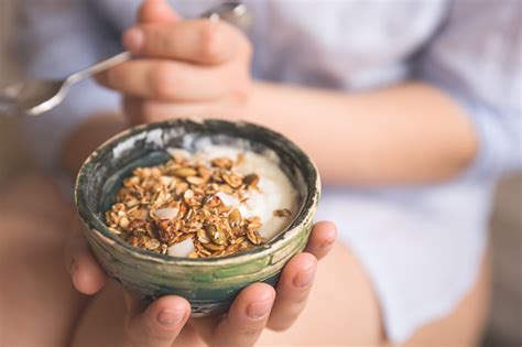 Muesli 그릇으로 젊은 여자 그릇에 아침 시리얼에 견과류 호박 씨앗 귀리와 요구르트를 먹는 여자 여자 잡고 만든 놀라 건강 한 간식 또는 아침에 아침 식사입니다