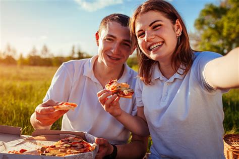 젊은 커플 밖에 서 피자 먹고 Selfie 복용 여자와 남자 석양 피크닉 데입니다 얘 들 아 재미입니다 건강에 좋지 않은 음식에