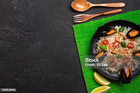 해산물 홍합 새우 바질이 있는 새단밥 나무 숟가락을 곁들인 검은 접시에 바질 녹색 대나무 매트와 돌 탁자 위에 포크 끓는 물에 삶기에 대한 스톡 사진 및 기타 이미지