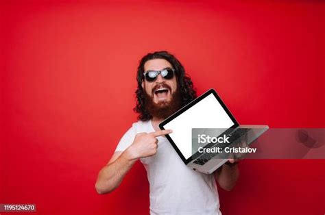 빨간 배경 위에 빈 노트북 컴퓨터 화면을 보여주는 쾌활한 수염 남자의 Portrit 승리 동작 활동에 대한 스톡 사진 및 기타 이미지 승리 동작 활동 매우 기쁜