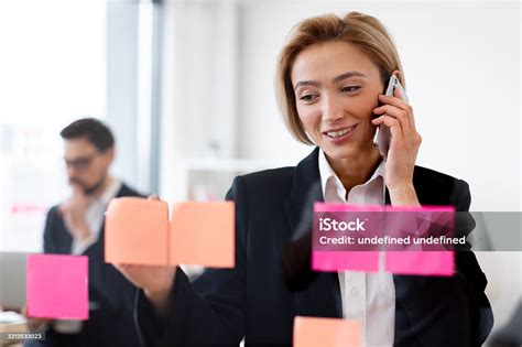 전화하는 여성 사업가는 사무실 유리 보드에 스티커 메모를 사용하여 작업을 정리합니다 30 34세에 대한 스톡 사진 및 기타 이미지 30 34세 35 39세 Brand